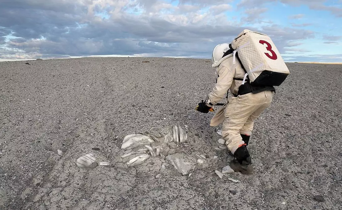 Ang isang mananaliksik sa isang spacesuit ay kumukuha ng mga sample mula sa isang deposito ng mga mahahalagang mineral sa Gemini Hills Plain.