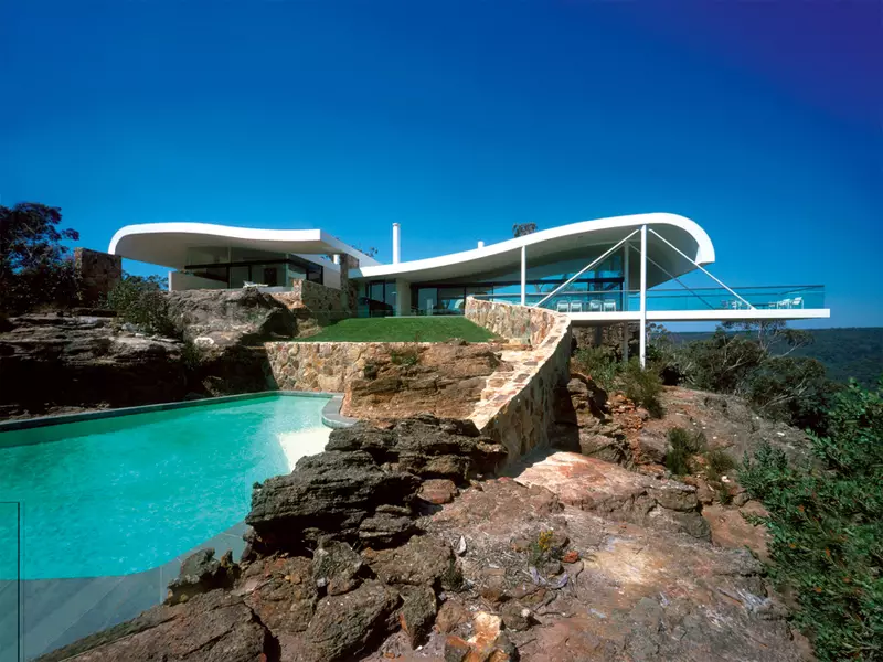 Berman Joage House, Australia Rodeada de una exuberante vegetación salvaje, esta sorprendente casa de dos pisos se equilibra en la cima de dos acantilados ligeramente diferentes en altura. Su estabilidad es proporcionada por largas repisas-balcones, que se extienden justo por encima del fondo de un profundo desfiladero, que, por costumbre, debe asustar al diablo. Y por la noche en esta zona deshabitada, los perros dingo aúllan, haciendo que el ambiente sea aún más inquietante.