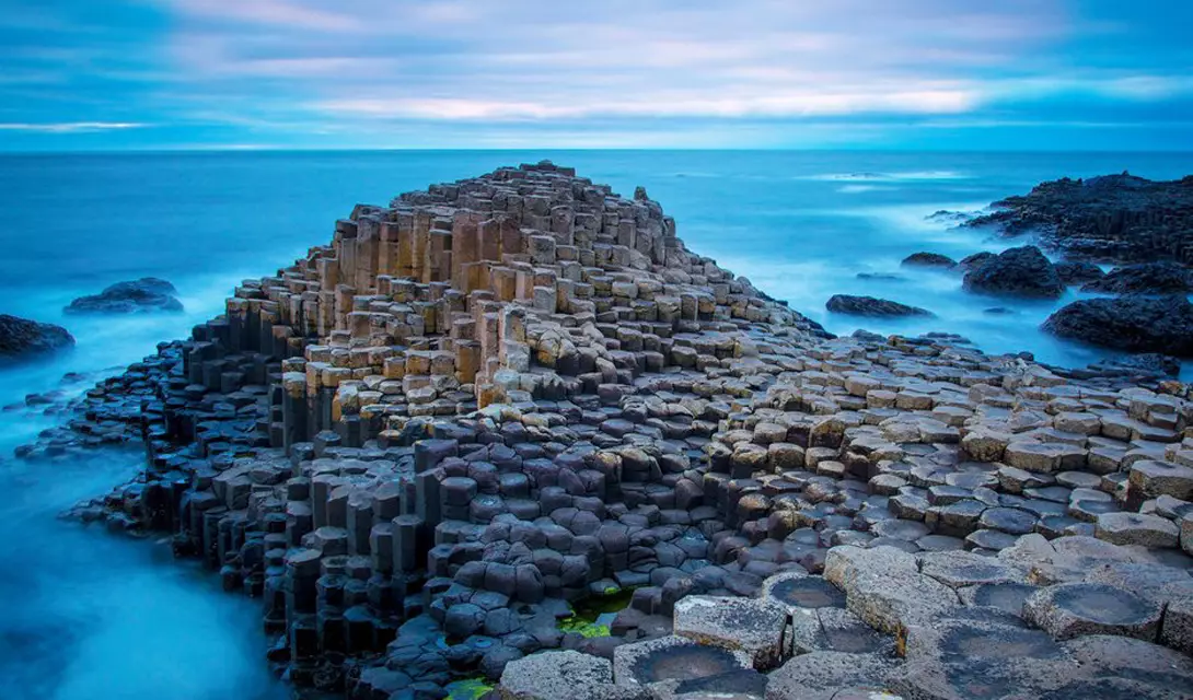 Causeway Coastal Route Түндүк Ирландия Миңдеген алты бурчтуу базальт мамылары Одиндин жана башка кудайлардын каарынан бул жерден өткөн троллдордун көпүрөсү деп эсептелет. Чындыгында, бул таң калыштуу тоо тектеринин пайда болушу жанар тоонун атылышынын натыйжасы.