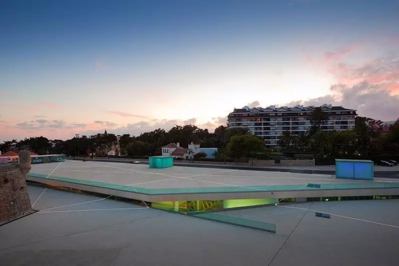 Tempat Parkir Bawah Tanah Cascais, Portugal Tidak jauh dari tembok batu abad pertengahan yang tersisa dari benteng tetangga, di kota Cascais, tepat di bawah alun-alun kota, ada tempat parkir bawah tanah yang besar. Itu dirancang oleh Arquitectos Associados. Strip LED terang yang menghiasi tempat parkir dengan lucu menyerupai peta navigasi kuno, sementara tangga tembus cahaya menerangi dinding benteng kuno saat senja.