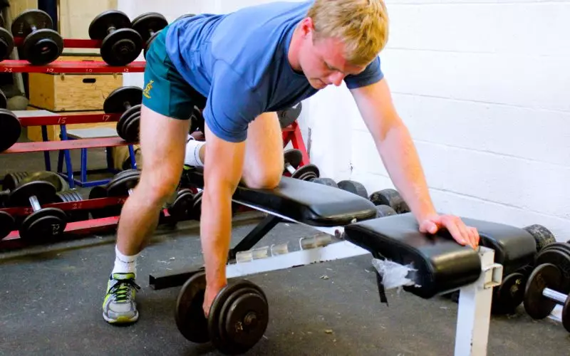 Yunamye hejuru ya Dumbbell Row Kugirango ukore umurongo hejuru, uzakenera intebe. Shira ivi ry'ibumoso n'ibumoso bwawe ku ntebe hanyuma ufate ikiragi mu kuboko kwawe kw'iburyo. Shira ikiganza cyawe hamwe na dumbbell hasi hanyuma, mugihe uhumeka, uzane ku kibero cyawe. Menya neza ko ikiganza kigwa hasi hashoboka mugihe cyo kugenda. Ibi bizarambura kandi bikomeze imitsi yinyuma.