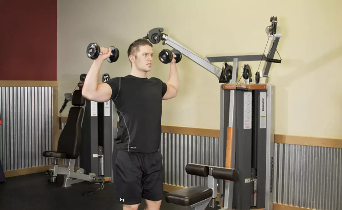 Standing Dumbbell Press Maaaring mukhang doble ng dumbbell press ang nakatayo na barbel press, ngunit hindi. Nang walang bar, ang hanay ng paggalaw ay tumataas nang malaki: binabaan mo ang iyong mga braso nang mas mababa, aktibong kinasasangkutan ng mga gitnang poste ng mga delta.