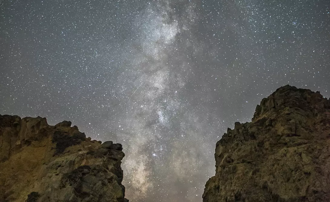 Eo anelanelan'ny vatolampy, ny Milky Way dia mamelatra ny lanitra amin'ny alina eo anelanelan'ny hantsam-bato manjavozavo ao amin'ny Pfeiffer State Beach, akaikin'i Big Sur, Kalifornia.