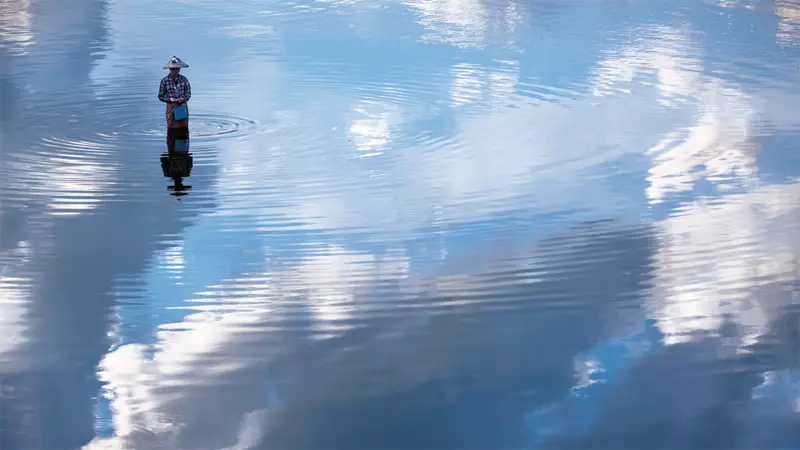 Donna durante la pesca. Una mattina, passeggiando lungo il famoso ponte U-Bane, costruito nel 1849 in legno di teak, David notò una donna al di sotto che stava pescando. Le nuvole si riflettevano nel lago, creando l'illusione che una donna stesse camminando nel cielo.